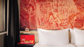 Quarto de hotel com um grande tapeçado vermelho na parede, uma cama com roupa de cama branca, uma mesa de cabeceira com um copo de água e um livro, e uma estante vermelha com um objeto decorativo.