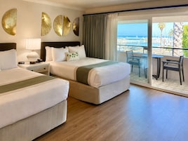 Quarto de hotel com duas camas, uma mesa de cabeceira, uma luminária e vista para a marina através de uma porta de vidro.