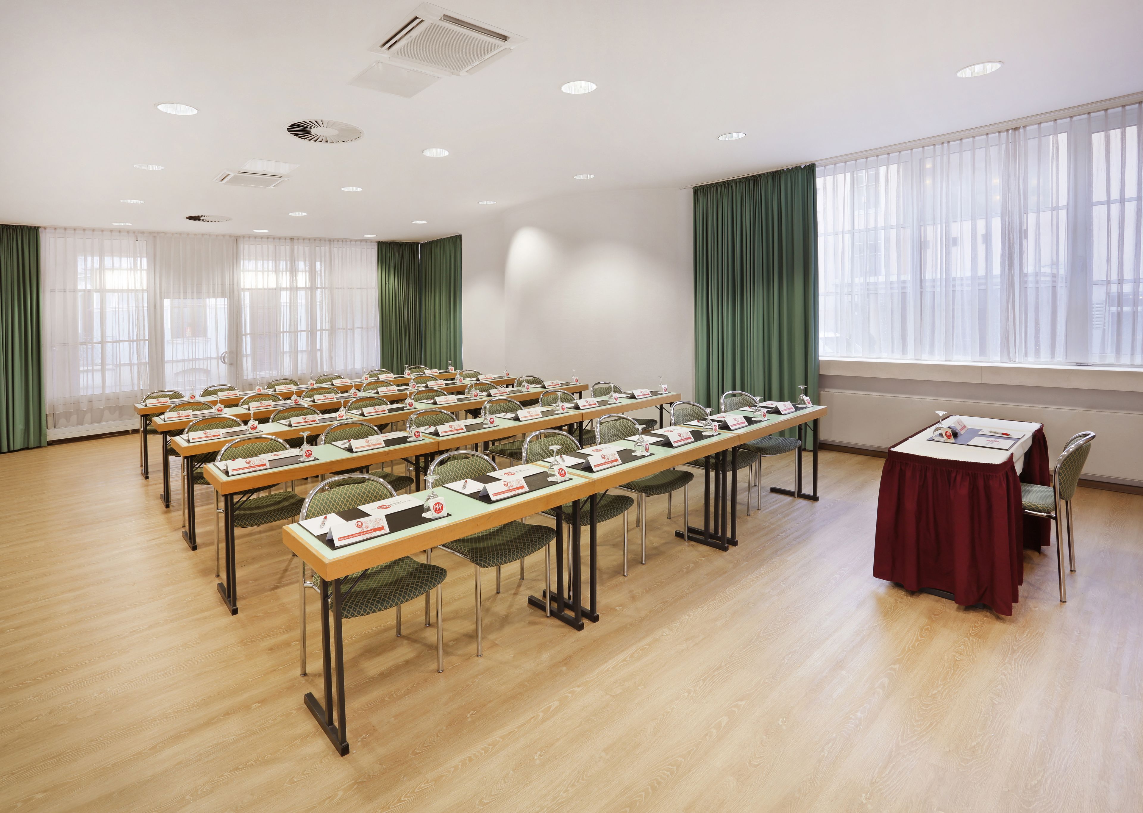 Uma sala de conferências com mesas compridas, cadeiras, placas de identificação e uma pequena mesa com toalha vermelha.