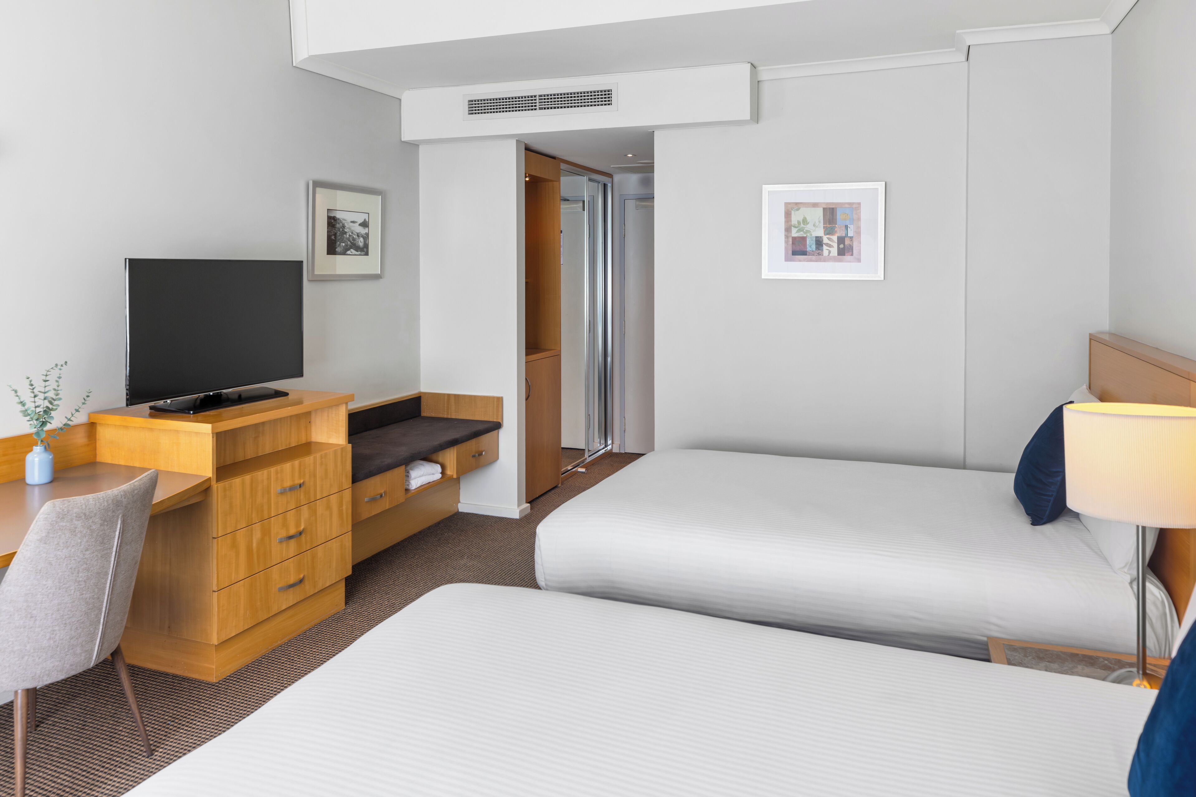 Quarto de hotel com cama, escrivaninha com televisão, guarda-roupa e porta de banheiro.
