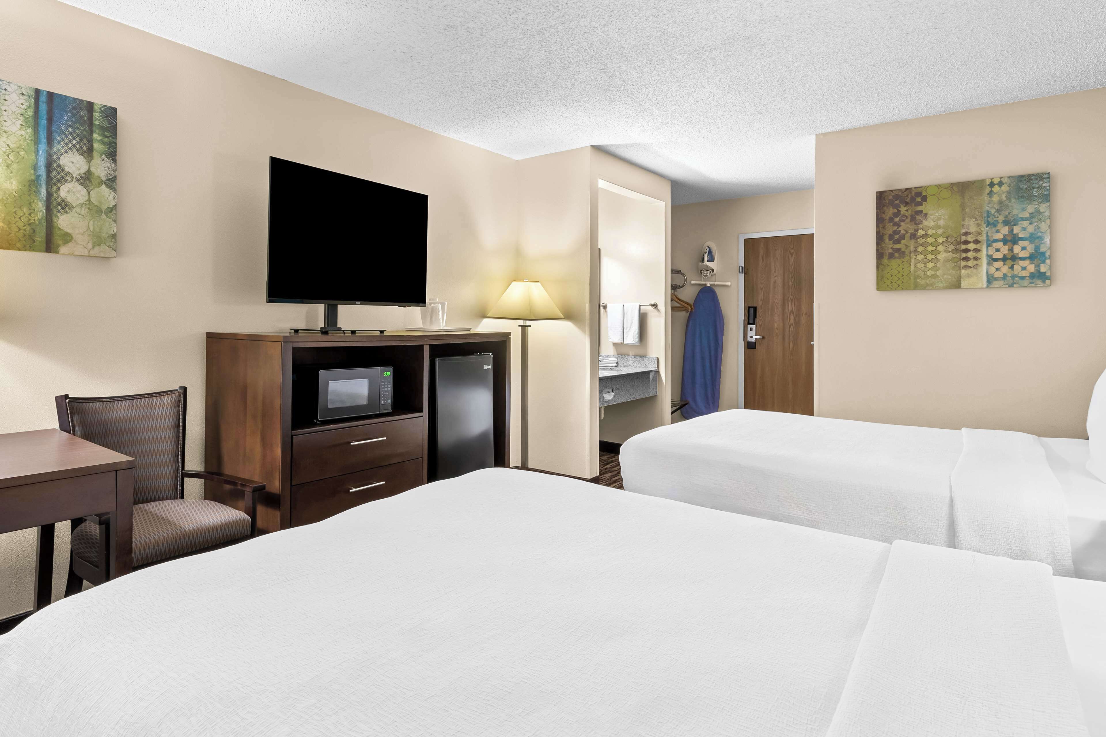 Quarto de hotel com duas camas, uma escrivaninha, televisão e guarda-roupa.