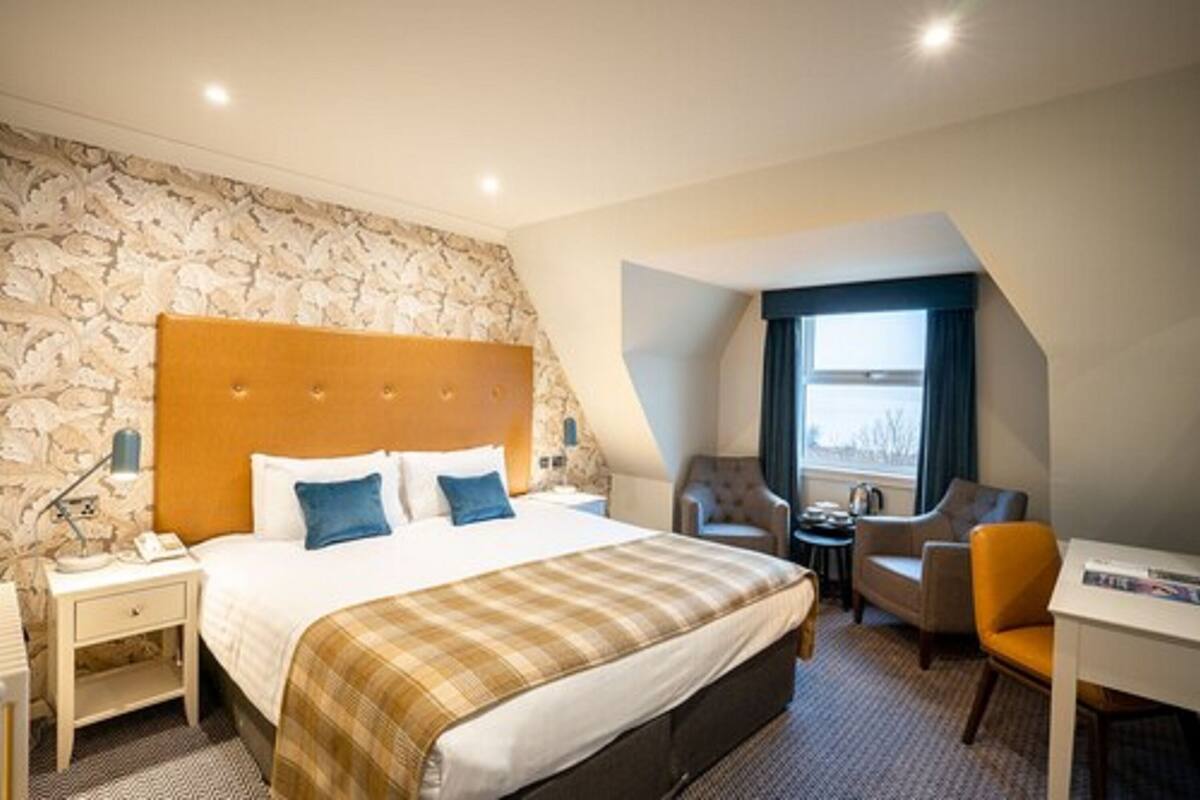 Quarto de hotel com uma cama grande, uma escrivaninha, uma cadeira e vista para o exterior.
