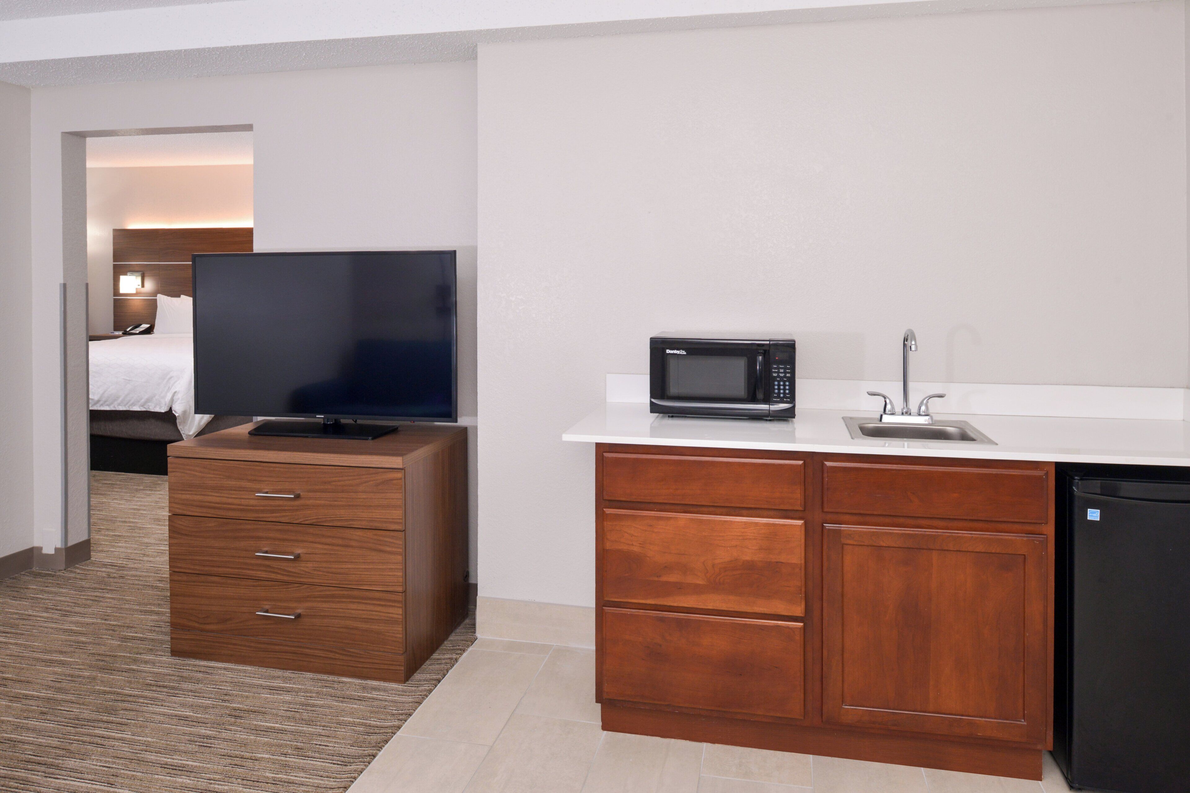Quarto de hotel compacto com cozinha compacta, televisão de tela plana, micro-ondas e pequeno frigorífico.