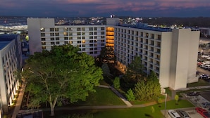 Hotel com vários andares e um pátio central, rodeado por árvores e um estacionamento.
