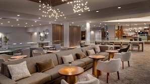 Um hall de hotel moderno com sofá em seção, mesas redondas e área de bar.