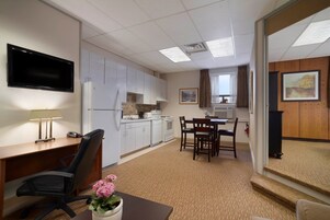 Quarto de hotel com escrivaninha, cadeira, cozinha compacta, área de refeições e televisão.