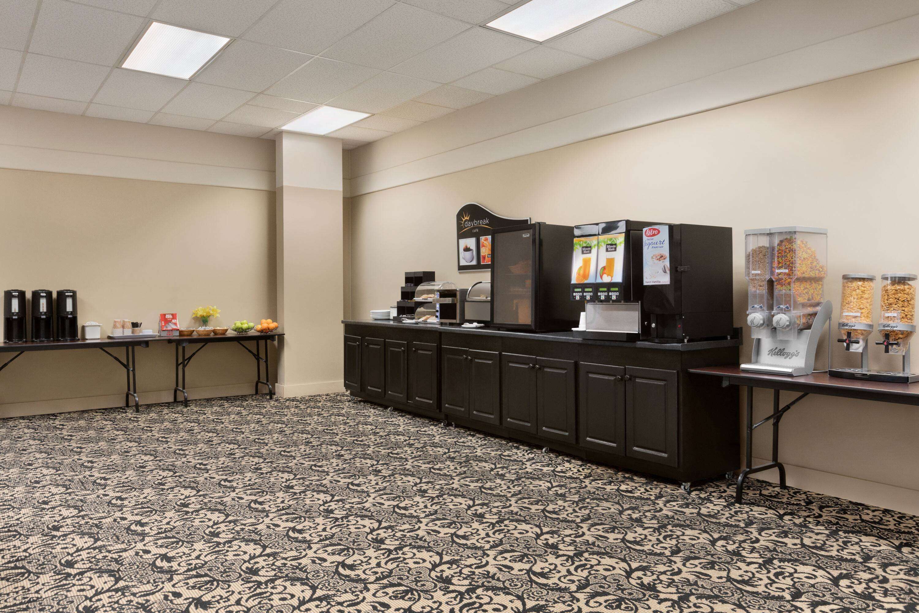 Uma sala de conferências com um espaço para café, mesa de buffet com frutas e lanches, e um tapete estampado.