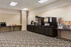 Uma sala de conferências com um espaço para café, mesa de buffet com frutas e lanches, e um tapete estampado.