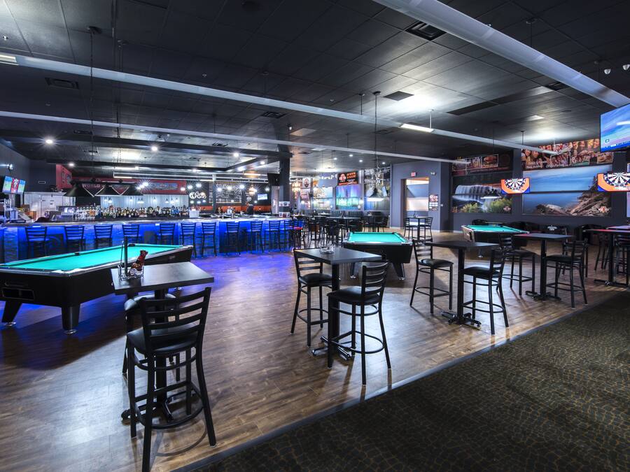Uma área de bar com mesas de bilhar, cadeiras e uma tela de televisão.