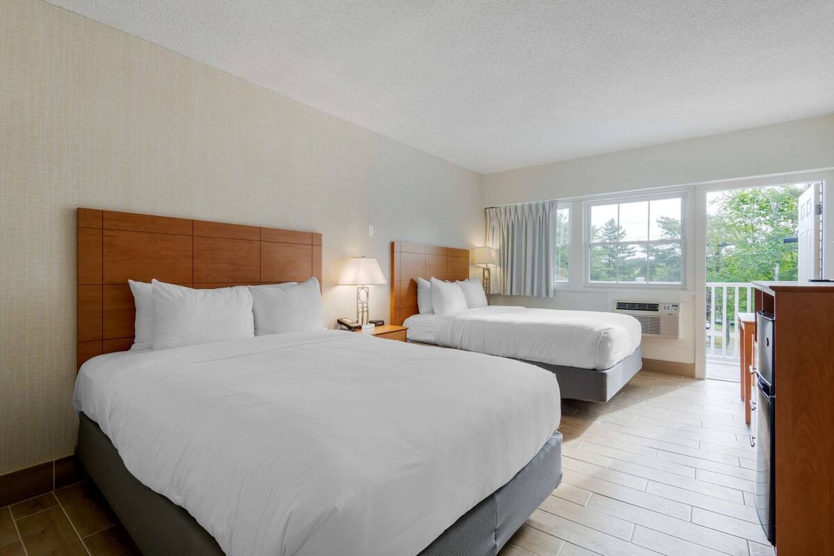 Quarto de hotel com duas camas, varanda e cozinha compacta.