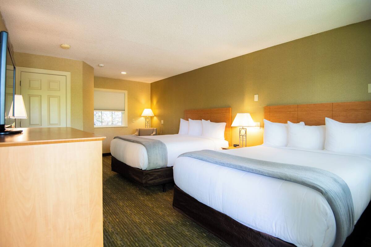 Quarto de hotel com duas camas, uma mesa e luminárias.