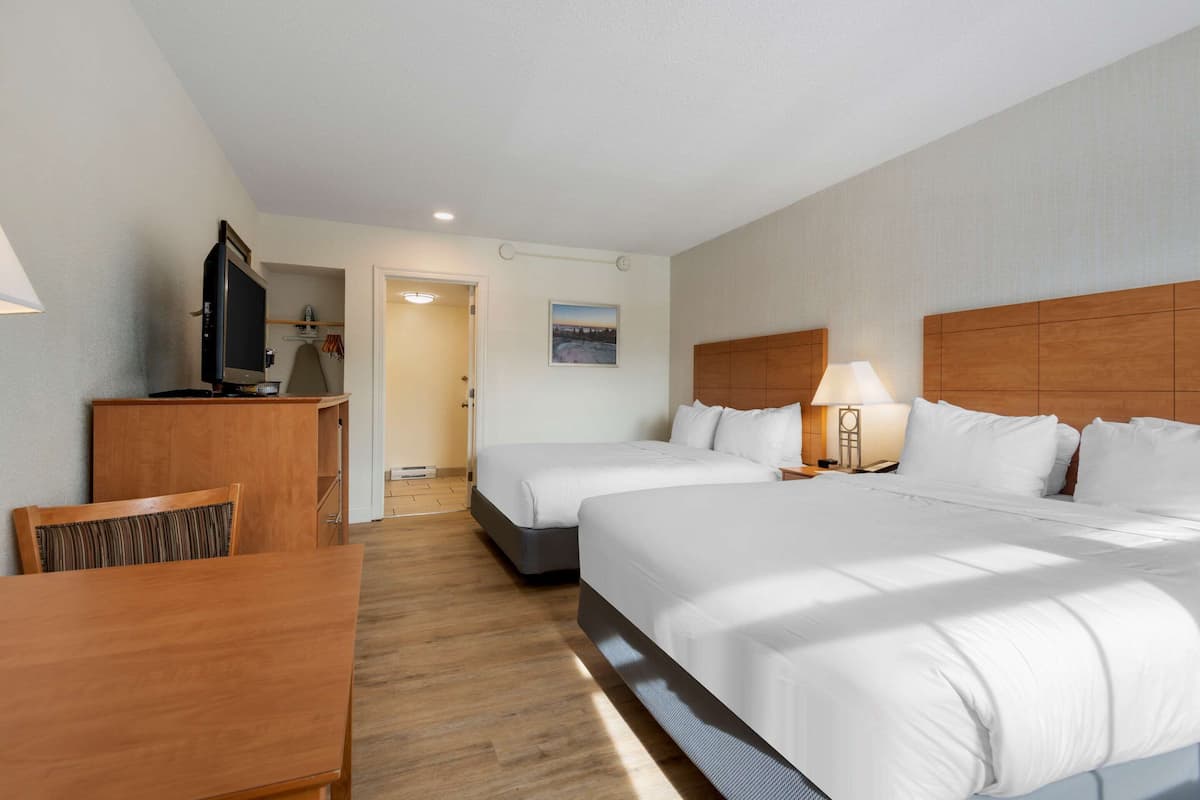 Quarto de hotel com duas camas, uma escrivaninha, televisão e porta que dá para um corredor.