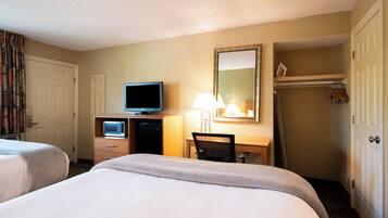 Quarto de hotel com duas camas, uma escrivaninha com televisão, abajur, espelho e guarda-roupa.