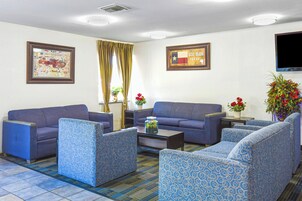 Um quarto com sofá azul, poltronas estampadas, mesa de centro e dois vasos de flores.