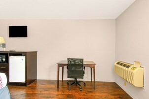Quarto com escrivaninha, cadeira, televisão na parede e ar condicionado.