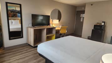 Quarto de hotel com uma cama grande, televisão, escrivaninha com cadeira, espelho e micro-ondas.