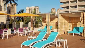 Área de piscina no terraço com espreguiçadeiras, guarda-sóis e vista para a paisagem urbana.