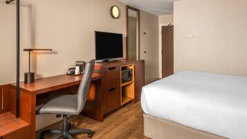 Quarto de hotel com secretária de madeira, televisão, cadeira, cama e micro-ondas.