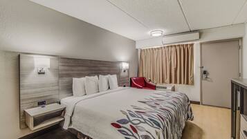 Quarto de hotel com cama, uma cadeira vermelha, escrivaninha e guarda-roupa.
