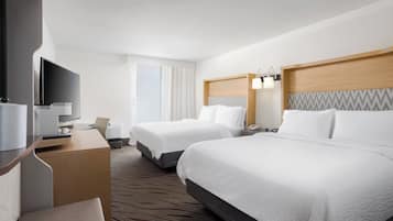 Quarto de hotel com duas camas, uma escrivaninha e televisão de tela plana, e uma janela grande com cortinas.