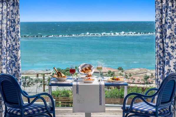 Mesa posta para dois com vista para o mar, duas cadeiras e toalha de mesa com bordado decorativo.