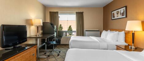 Quarto de hotel com duas camas, uma escrivaninha com televisão, uma cadeira e um abajur.