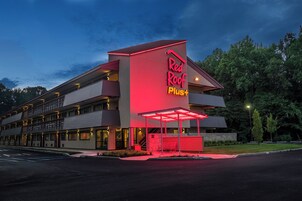 Hotel Red Roof Plus com design arquitetônico moderno, destacando uma placa grande nas cores vermelha e amarela, área externa coberta e estacionamento.