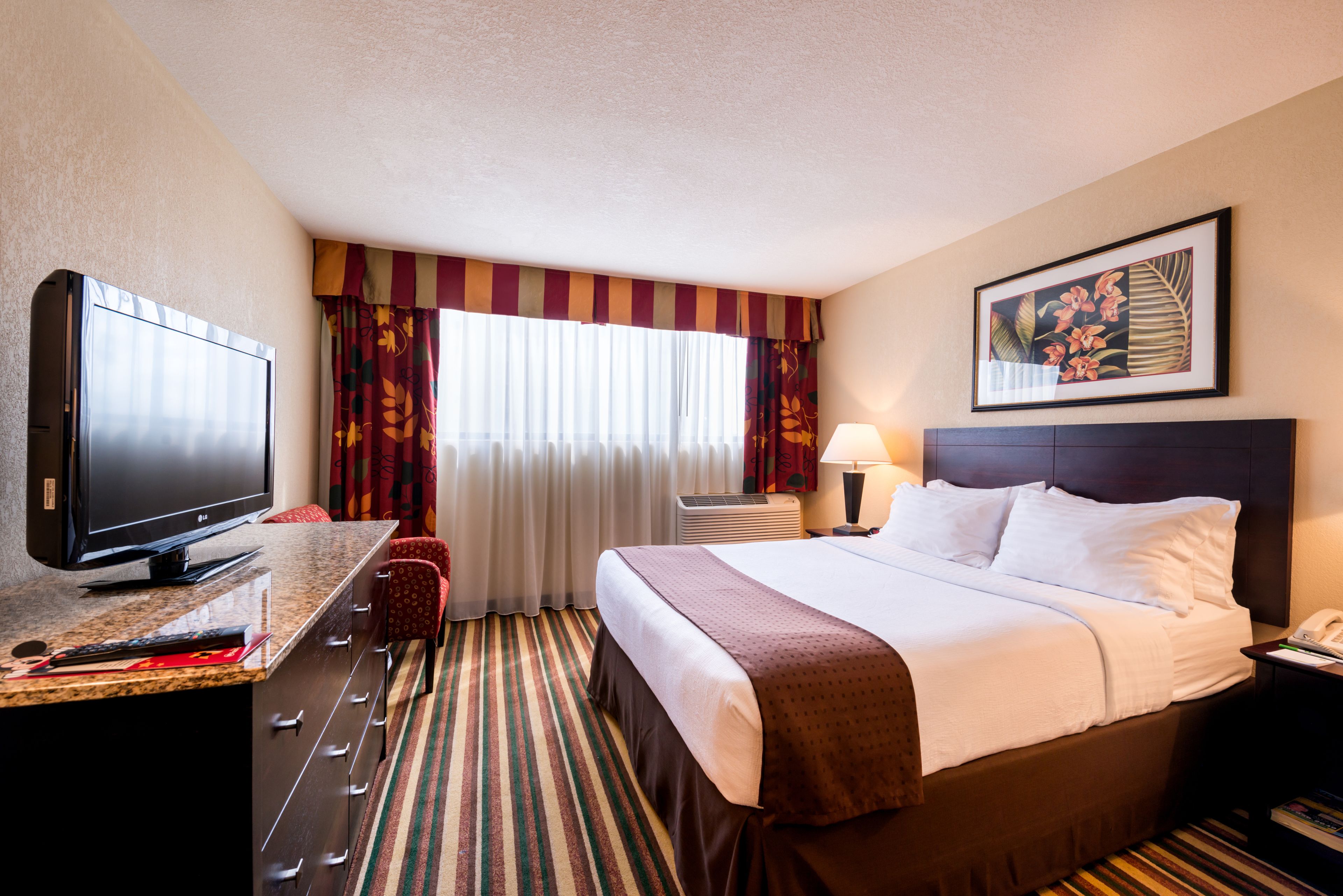 Quarto de hotel com cama, televisão, escrivaninha e cadeira.