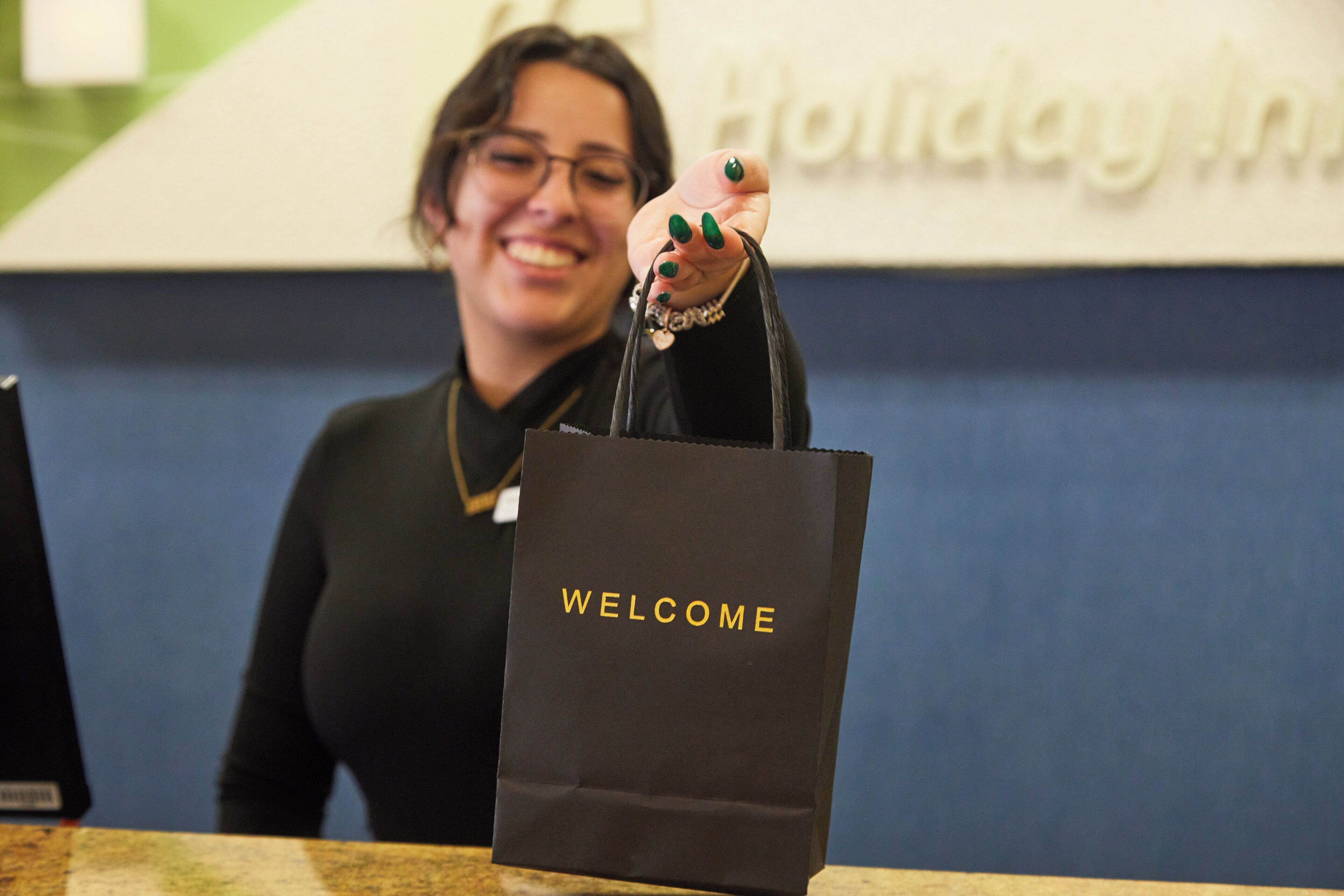 Uma pessoa segurando uma bolsa preta com a palavra 'WELCOME' escrita.