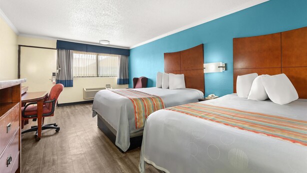 Quarto de hotel com duas camas, uma escrivaninha e uma cadeira.