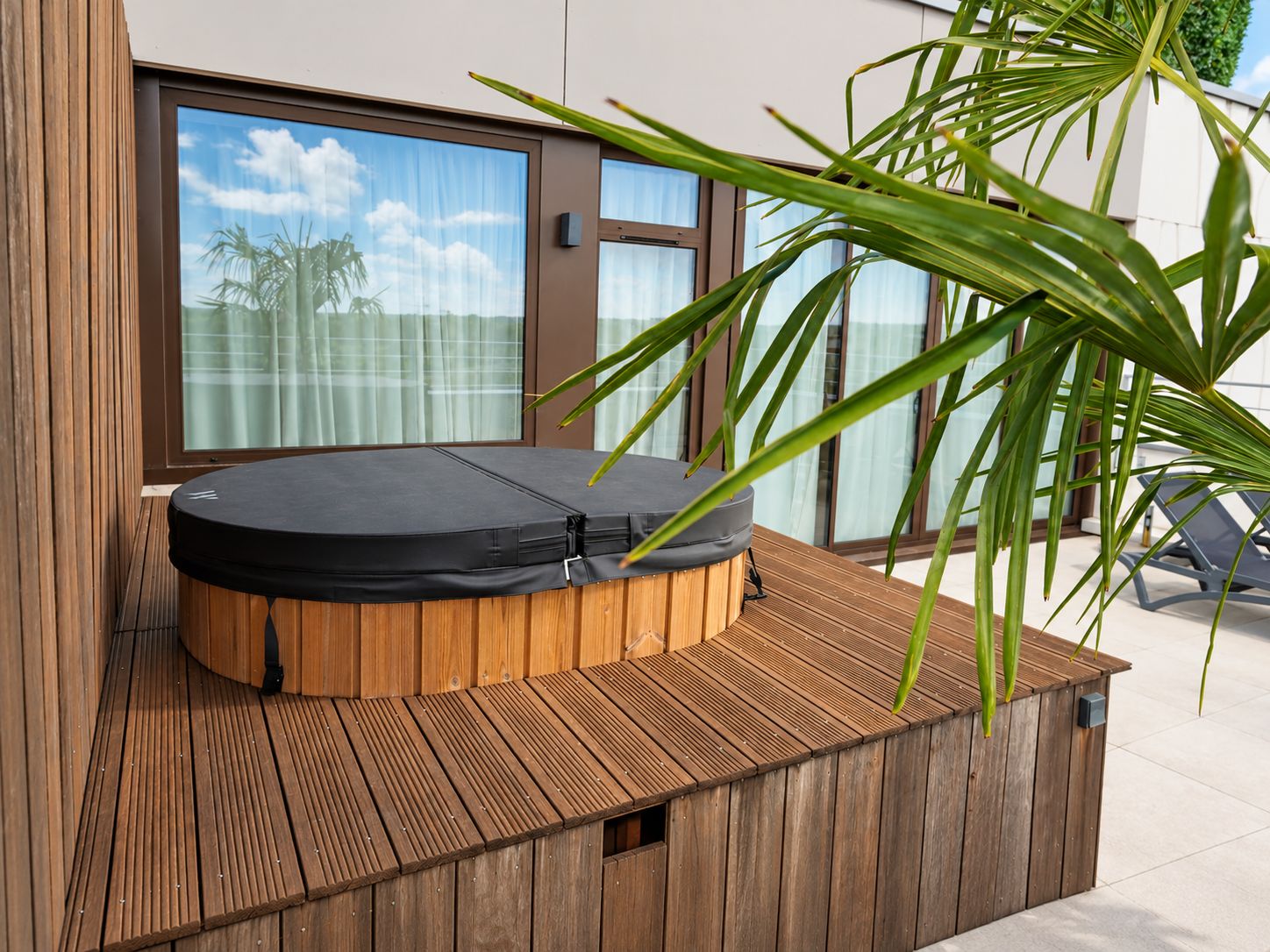 Um deck de madeira com hidromassagem, uma janela com cortinas e um vaso de planta.