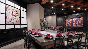 Um restaurante com uma mesa comprida para vários clientes, cadeiras pretas e guardanapos vermelhos.
