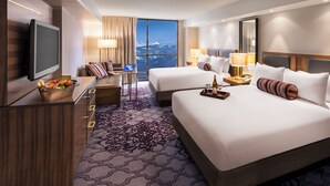 Quarto de hotel com duas camas, uma televisão, uma secretária com um computador portátil e vista para uma montanha nevada.