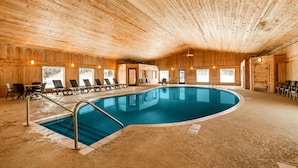 Piscina interior com paredes e teto de madeira, rodeada por espreguiçadeiras e uma pequena mesa.