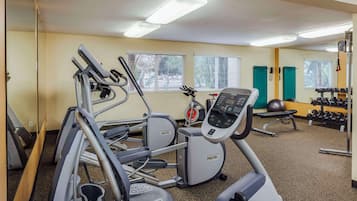 Uma academia com diversos equipamentos de cardio, halteres e um banco.