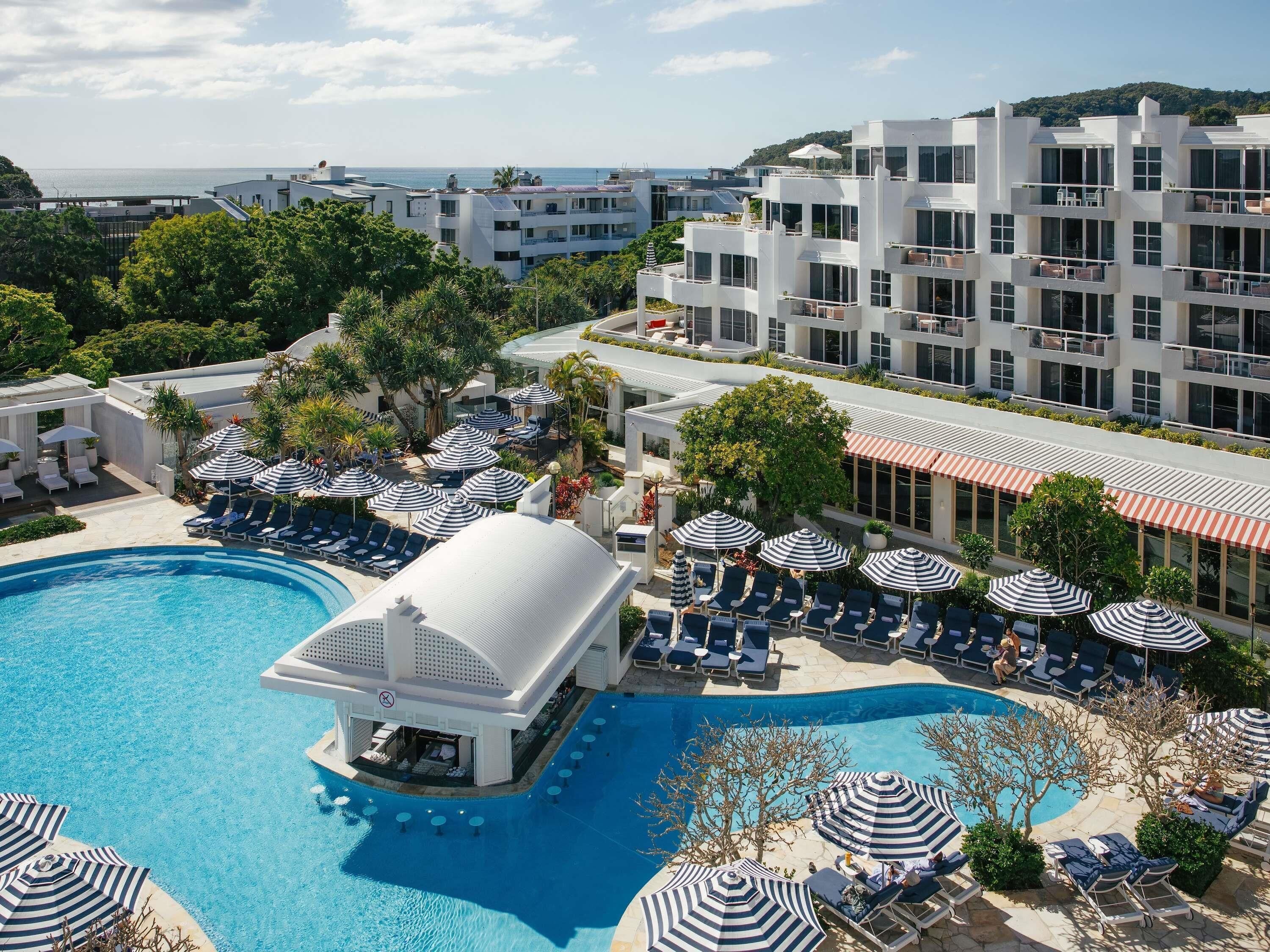 Um resort com piscina, espreguiçadeiras, guarda-sóis e vista para o mar.