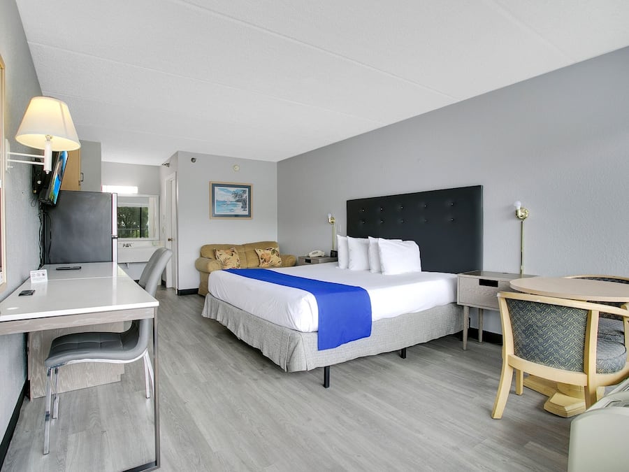 Quarto de hotel com cama, escrivaninha, cadeira e uma pequena mesa redonda também com uma cadeira.