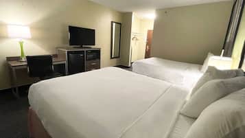Quarto de hotel com duas camas, uma escrivaninha com televisão, um espelho e um abajur.