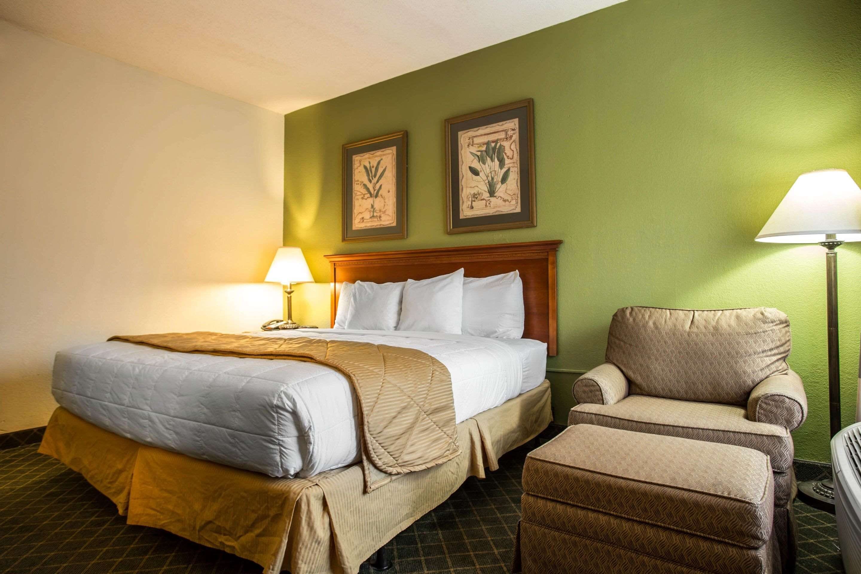 Quarto de hotel com uma cama grande, uma cadeira e duas luminárias fixadas na parede.