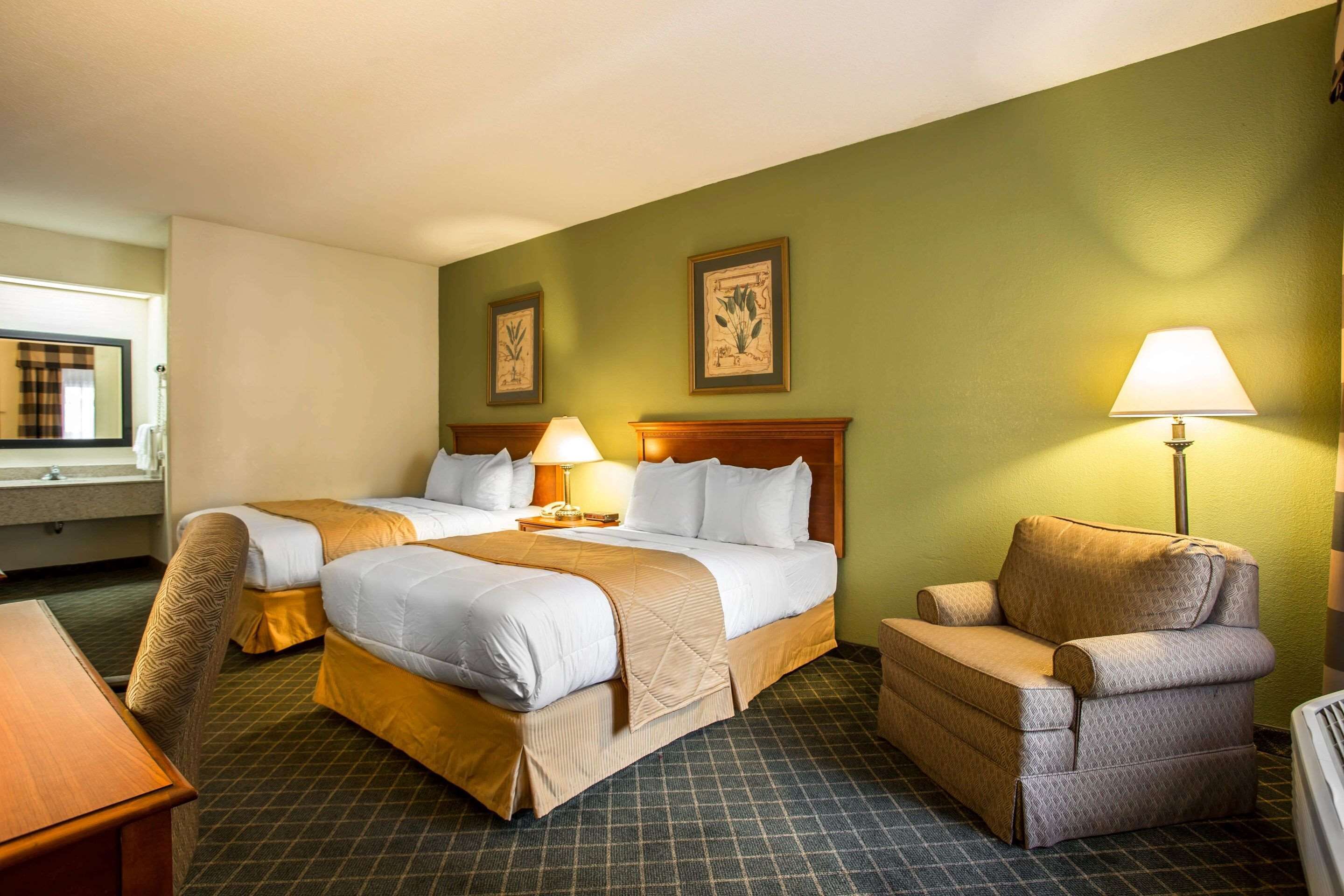 Quarto de hotel com duas camas, um sofá, uma escrivaninha e um abajur.