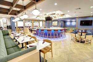 Restaurante com área de bar, diversas opções de assento incluindo cabines e mesas, e uma televisão fixada na parede.