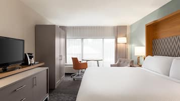 Quarto de hotel com uma cama grande, televisão, escrivaninha com luminária e uma cadeira.