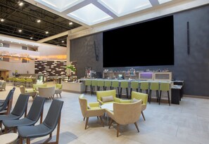 Espaço moderno em ambiente interno, com área de bar, assentos e uma tela grande.