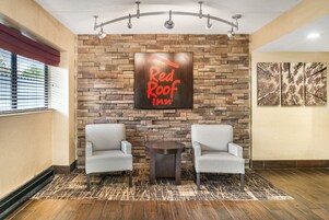 Lobby de um Red Roof Inn com parede de pedra, dois poltronas, uma mesa pequena e um ventilador de teto.