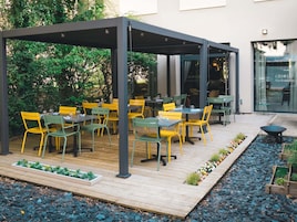 Uma área de pátio externa com mesas e cadeiras, um espaço coberto para sentar e um jardim com plantas e um recurso de água.