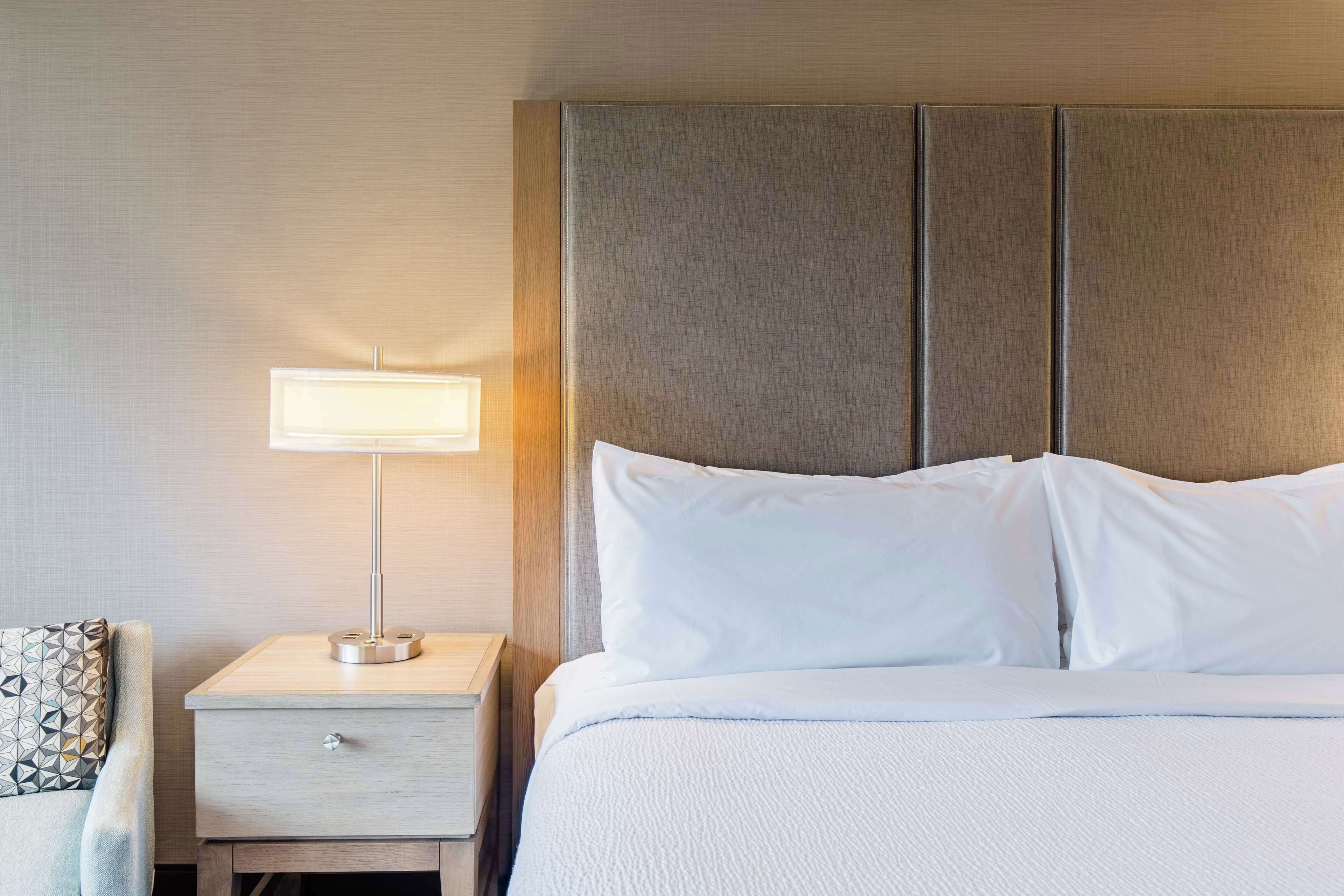Quarto de hotel com uma cama, mesa de cabeceira e abajur.