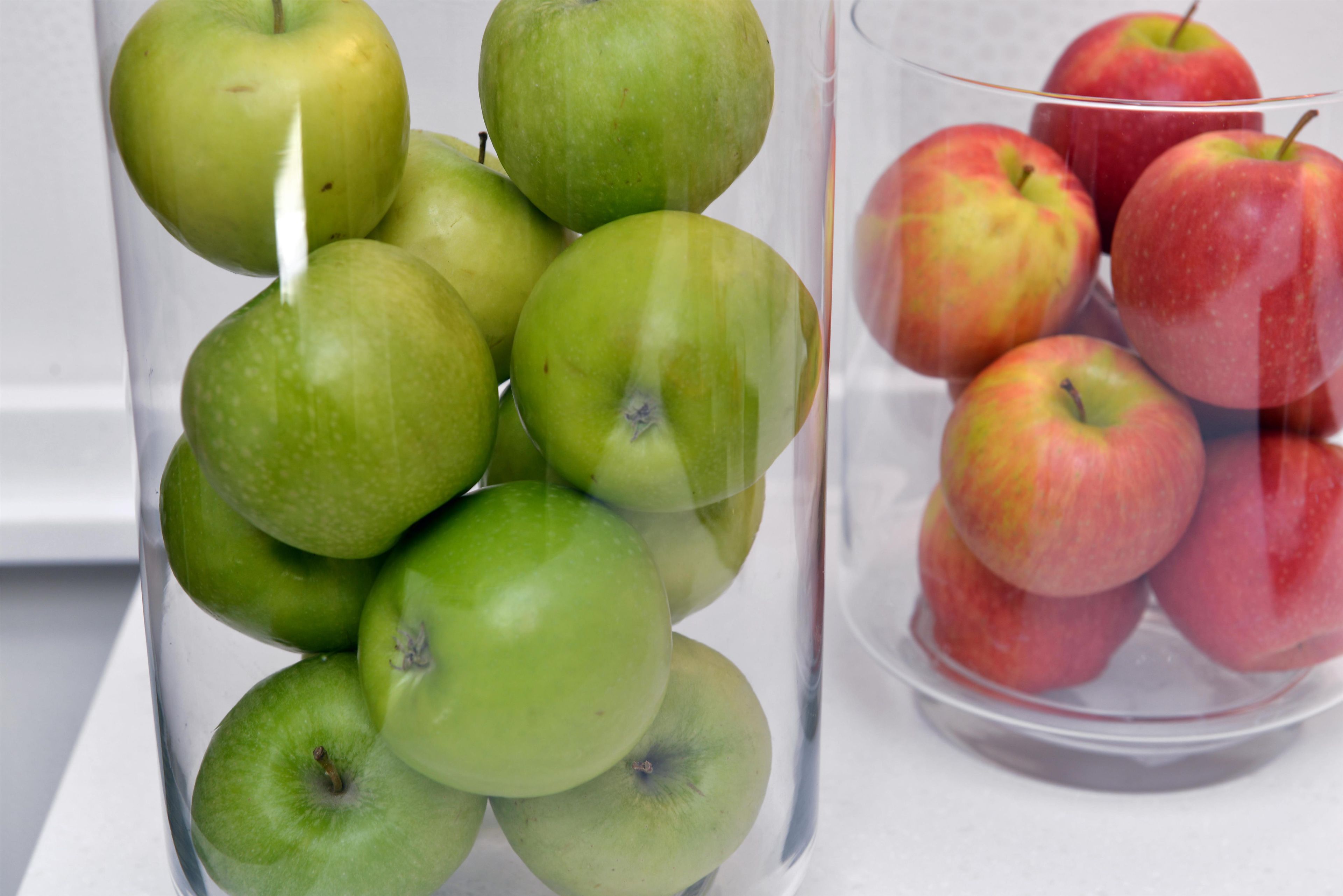 Recipiente de vidro transparente com maçãs verdes à esquerda e maçãs vermelhas à direita.
