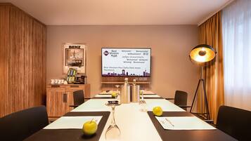Sala de conferência com uma mesa comprida, cadeiras, relógio, placa de boas-vindas emoldurada e abajur.