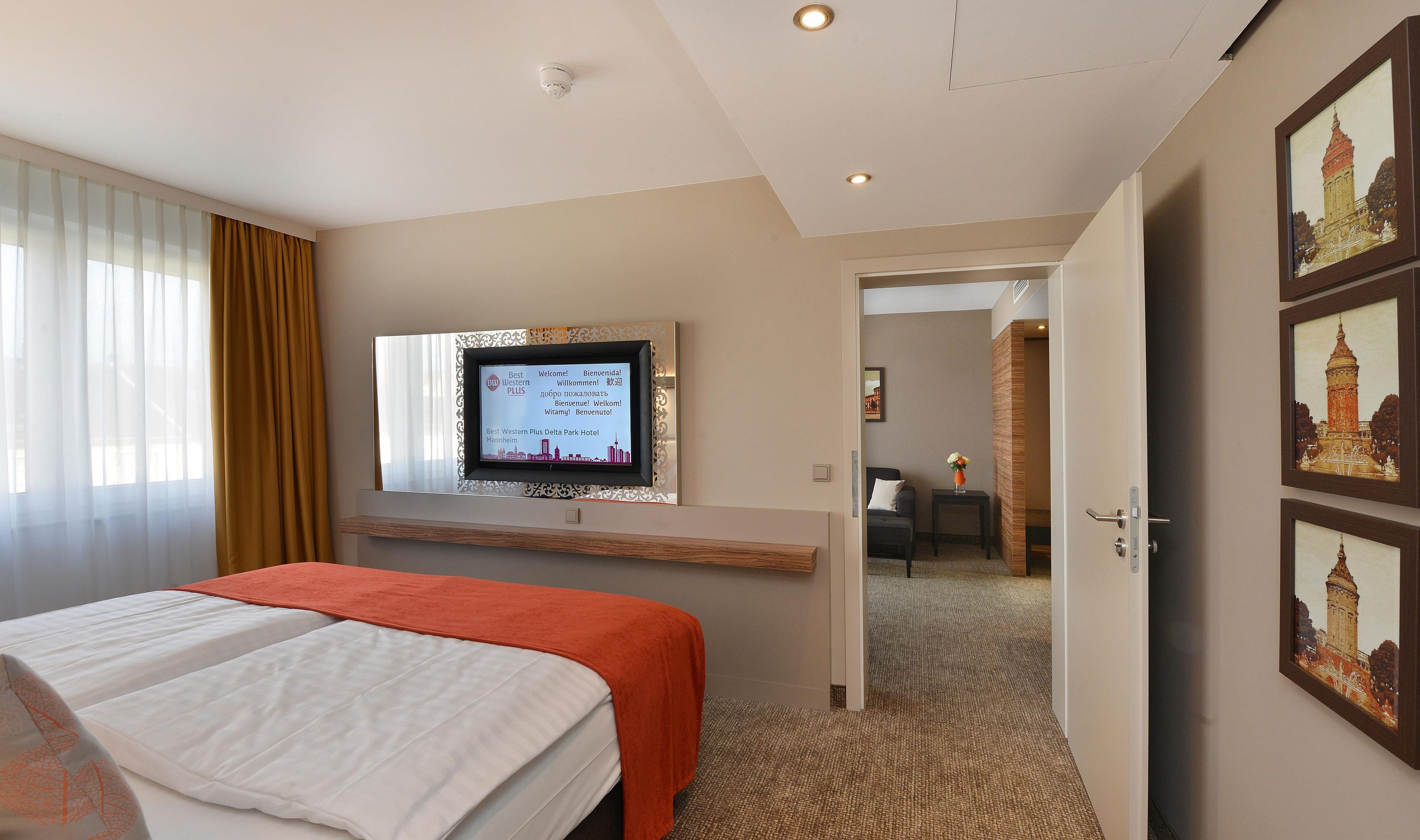 Quarto de hotel com uma cama, televisão na parede e porta para um corredor.
