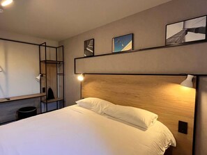 Quarto de hotel moderno com beliche, mesa de cabeceira, espelho e obra de arte na parede.